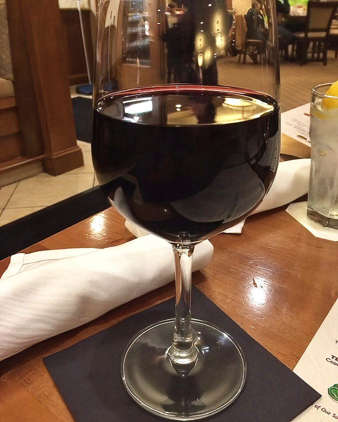 A glass of ruby-red wine catching the light just so&mdash;because sometimes a sandwich this good deserves a proper toast.