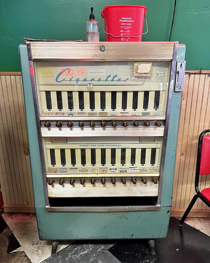 This vintage cigarette machine stands as a museum piece from another era, now repurposed beside modern hand sanitizer&mdash;old meets new.