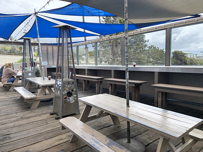 Simple wooden picnic tables under blue sail shades—because fancy furniture would just distract from the food and views.