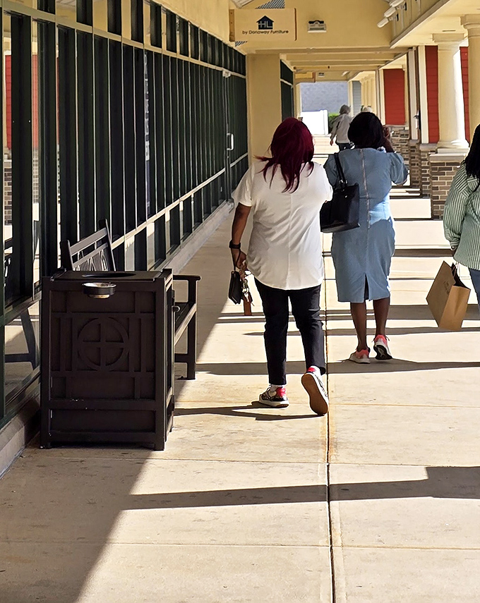 Savvy shoppers navigate the sun-dappled walkways between stores, bags in hand, embodying the thrill of the hunt that makes outlet shopping a competitive sport.