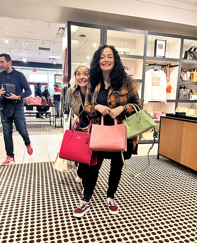 Happy shoppers showing off their colorful handbag treasures. The universal expression of "Wait until I tell everyone what I paid for this!"