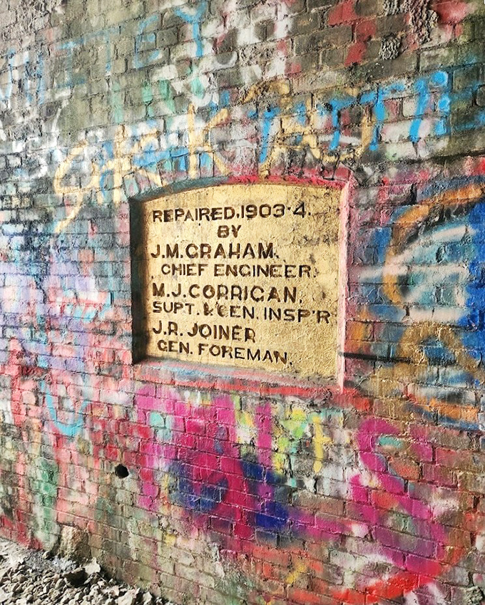 This 1903 repair plaque, surrounded by modern graffiti, creates a striking visual timeline spanning over a century of human presence.