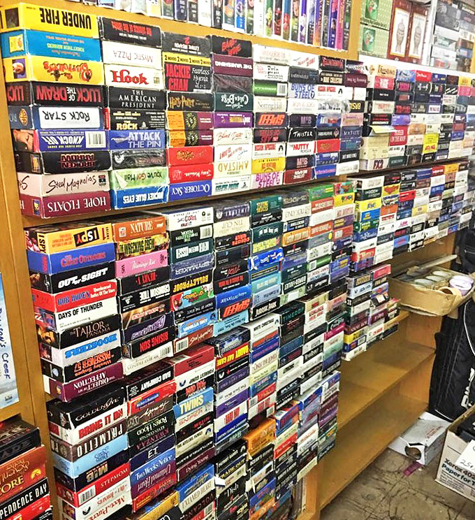 VHS tapes stacked like a physical Netflix from another era&mdash;each spine a portal to movie nights before streaming, when "be kind, rewind" was our mantra.