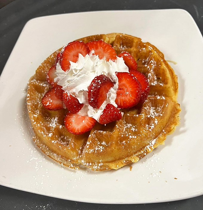Breakfast doesn't get more indulgent than a golden waffle crowned with fresh strawberries, whipped cream, and a dusting of powdered sugar.