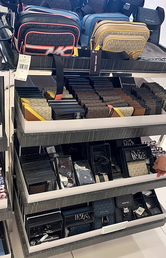 Designer wallets and accessories arranged with museum-like precision &ndash; Michael Kors monograms standing ready to upgrade pocket contents from mundane to magnificent.