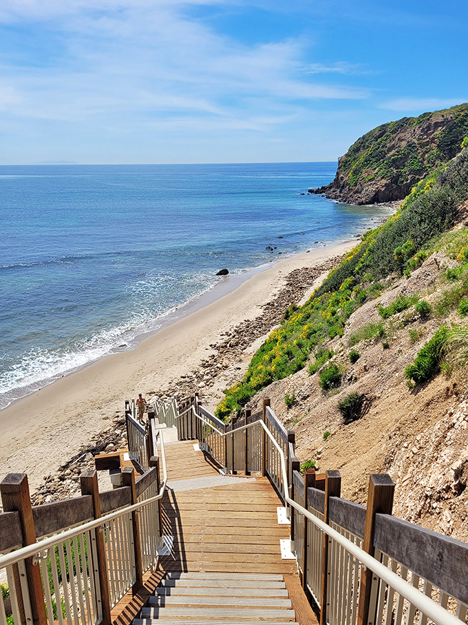 The wooden staircase descends like a promise, each step bringing you closer to that perfect stretch of sand that tourist brochures can only attempt to capture.