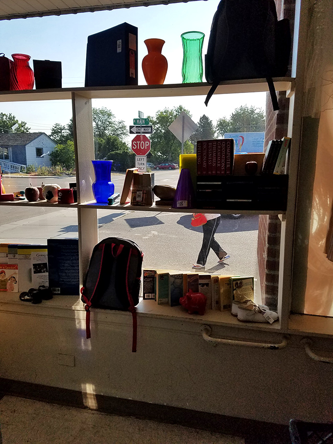 The view from inside reveals a world of colorful glassware catching the sunlight, while everyday life continues just outside the window.