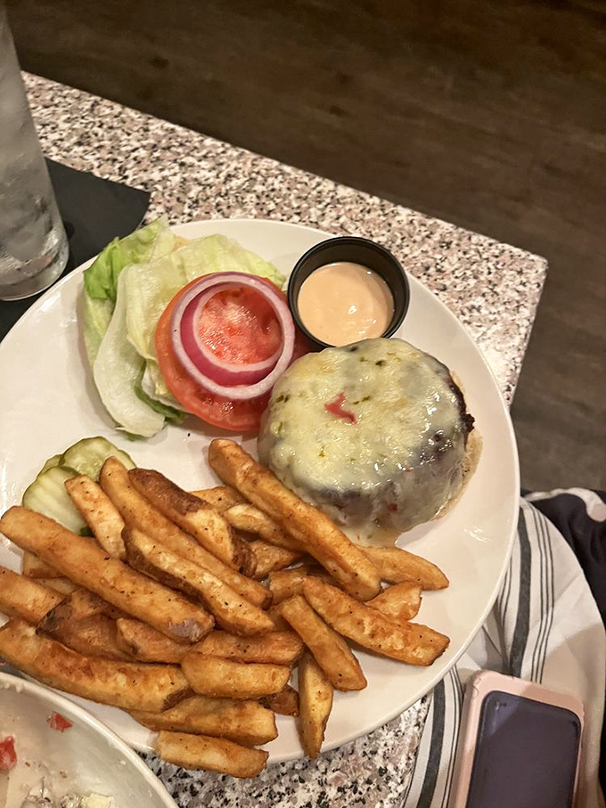 The burger arrives like a champion, cheese melting perfectly over the patty, with fries that achieve that mythical balance of crispy exterior and fluffy interior.