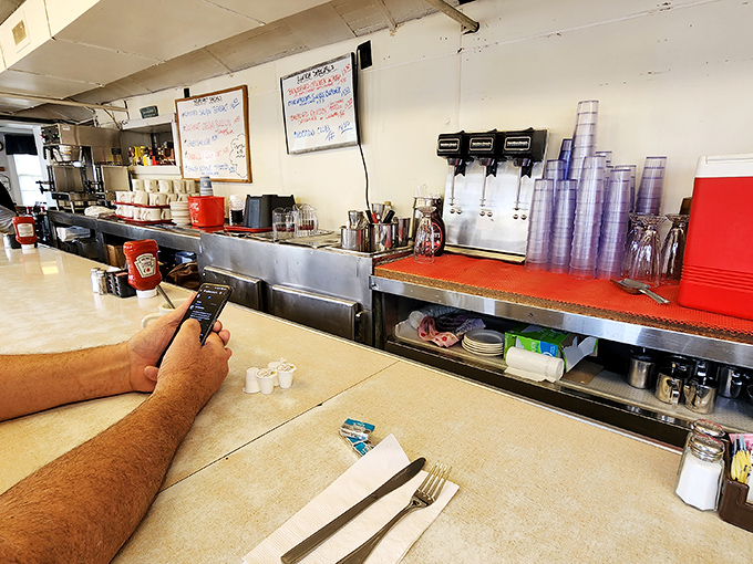The counter view—where regulars perch with newspapers and coffee refills flow like conversation in this command center of comfort food.