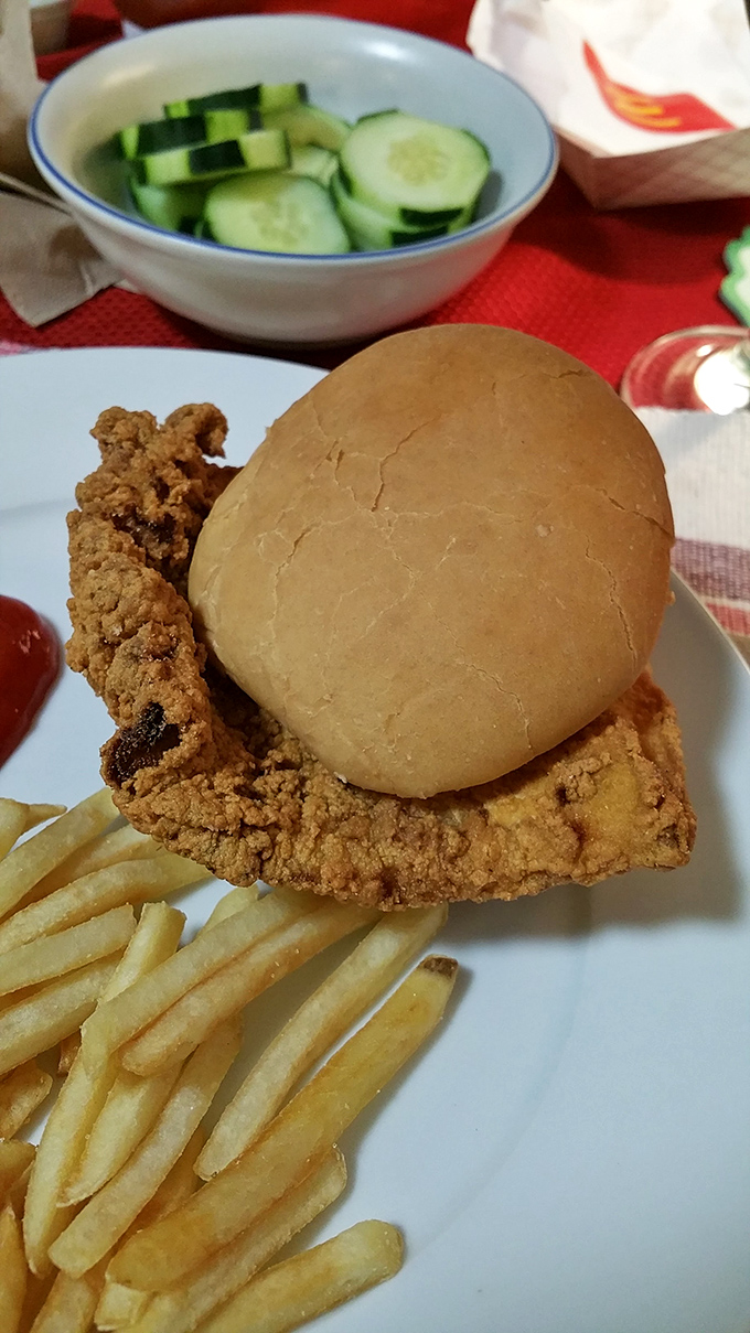 The fish sandwich laughs at the boundaries of its bun, crispy haddock extending well beyond bread borders in a delicious act of defiance.