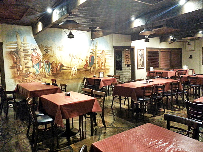 The cowboy mural watches over diners like a painted chaperone, silently approving your decision to order that second cocktail.