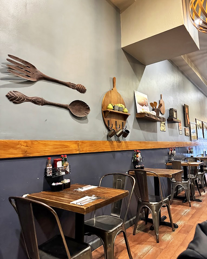 Rustic wooden tables beneath oversized utensil wall art – because subtle reminders of the eating experience are apparently necessary.