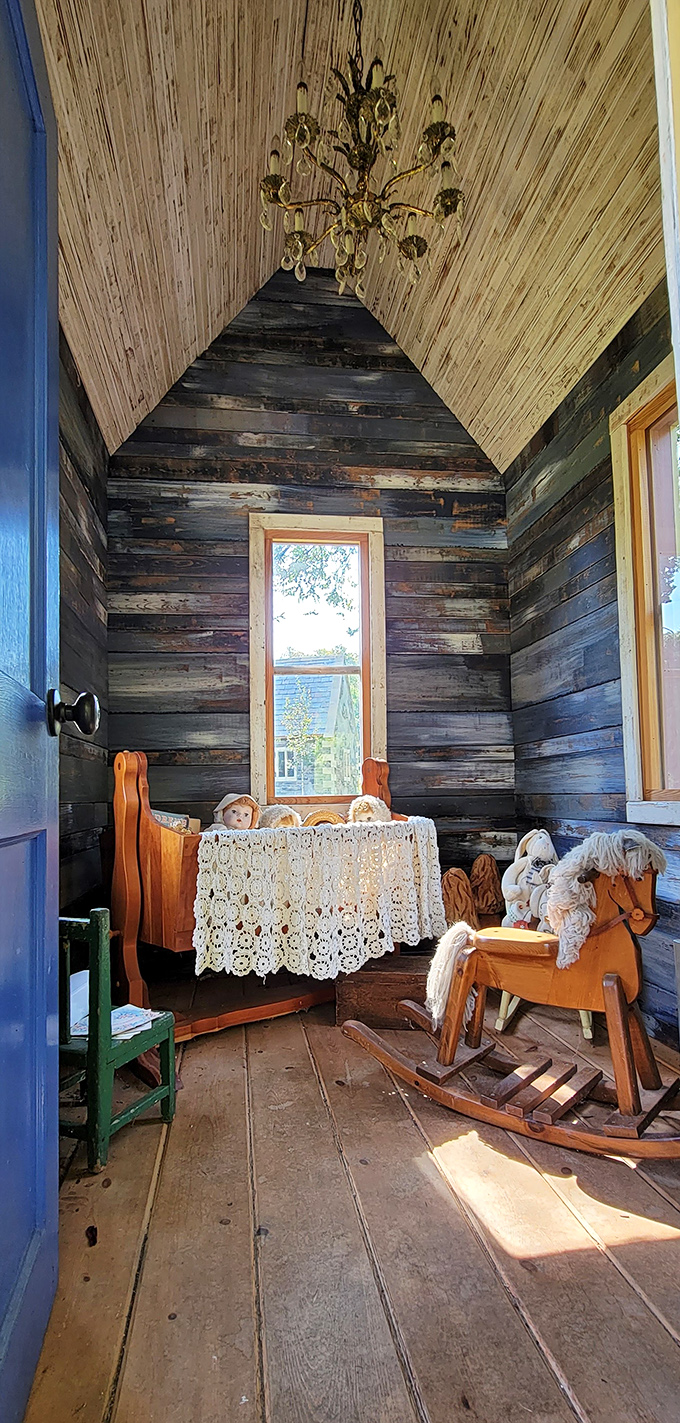 Rustic charm meets storybook nostalgia in this cabin interior, where a rocking horse and antique crib await beneath a crystal chandelier.