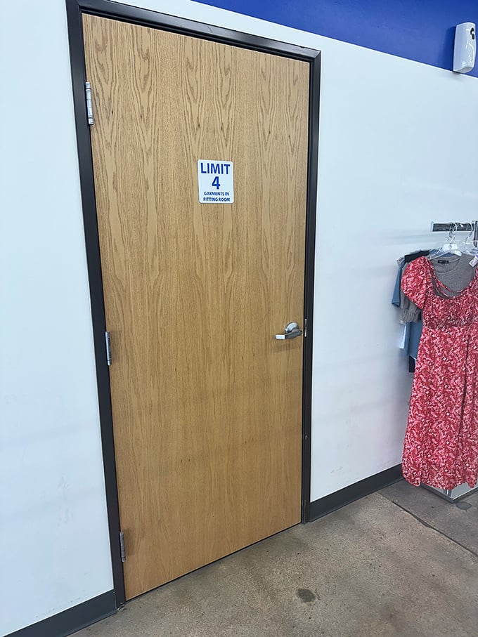 The fitting room door&mdash;gateway to possibility. Four garment limit means choosing wisely, like selecting contestants for a fashion reality show.