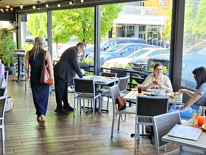 Sunlight streams through floor-to-ceiling windows onto the patio seating, where diners savor both their meals and the people-watching opportunities.