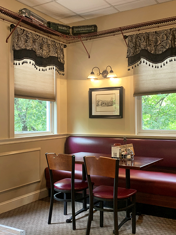 A model train circles above this cozy corner booth, where elegant window treatments frame views of greenery outside&mdash;transportation themes that go beyond decoration.