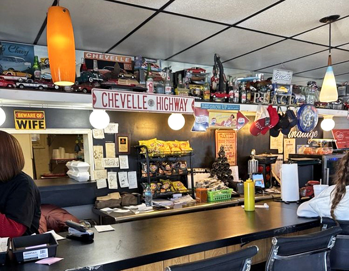 "Beware of Wife" signs and model cars line the shelves above the counter. This isn't corporate-designed nostalgia; it's the real, accumulated thing.