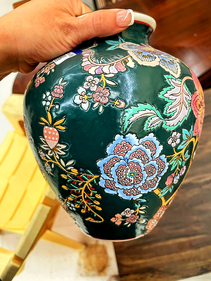 A hand cradles an intricately painted vase&mdash;someone's former treasure becoming your conversation piece. Floral artistry that never needs watering!
