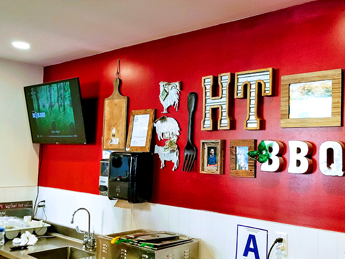 The vibrant red wall adorned with BBQ memorabilia serves as both decoration and mission statement – this place takes its meat seriously, but not itself.
