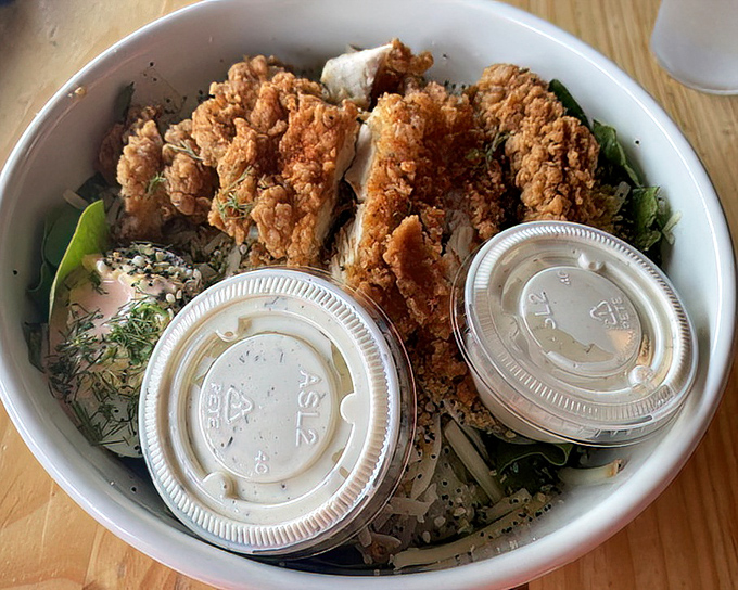 A bowl where crispy chicken and fresh greens coexist in perfect harmony. Those sauce containers hold liquid gold that transforms each bite.