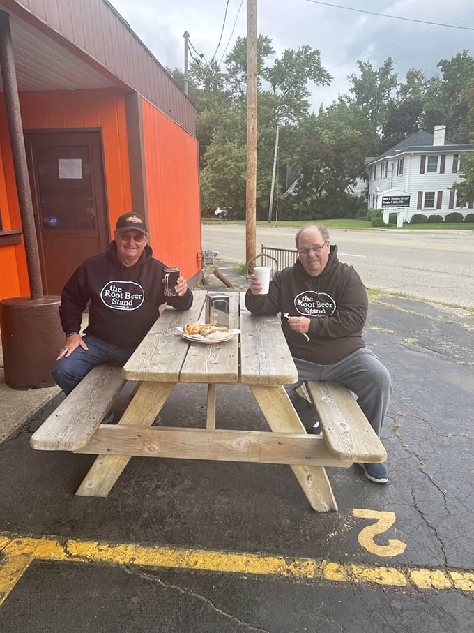 Two gentlemen who understand that some pleasures in life—like root beer and friendship—are best enjoyed outdoors at a weathered picnic table.