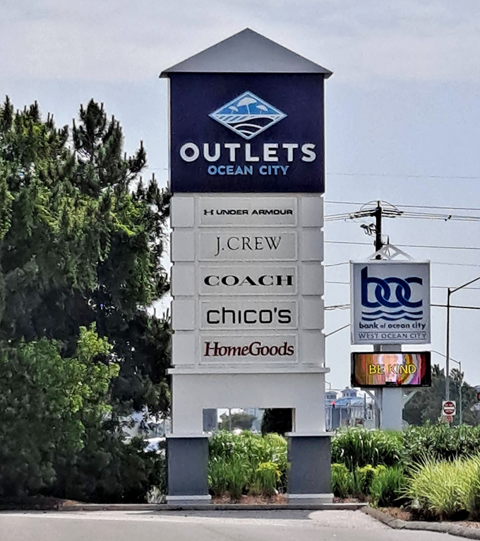The towering sign announces retail royalty with Under Armour, J.Crew, Coach, and more, standing like a lighthouse guiding bargain-seekers safely to discount shores.