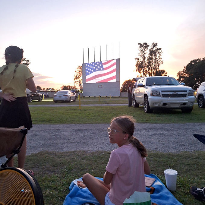 The pre-show ritual: blankets spread, drinks positioned, anticipation building as the American flag signals the start of a timeless tradition.