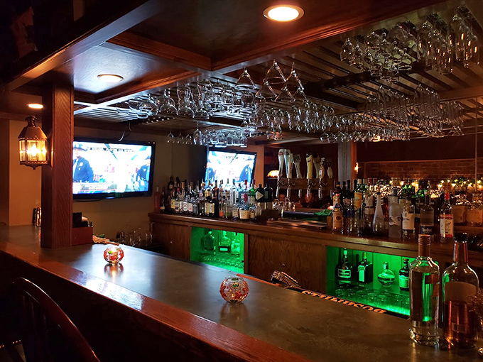 A bar that gleams with promise&mdash;hanging glasses catching the light like crystal chandeliers above that emerald-lit display.