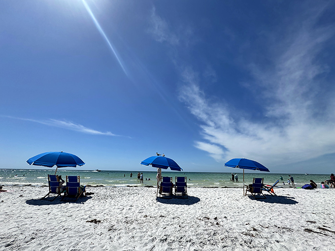 Three blue umbrellas standing guard over paradise. The beach chair rental that outperforms any five-star hotel lounger.