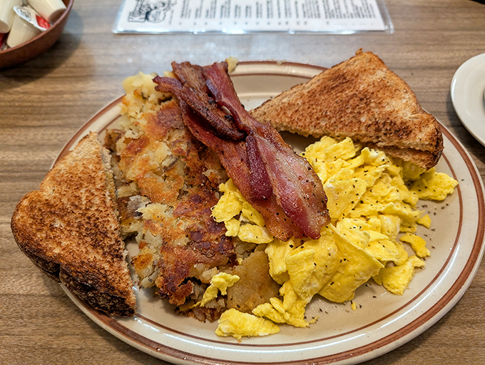 The breakfast trinity: perfectly scrambled eggs, golden hash browns, and toast that knows its supporting role but plays it with dignity.