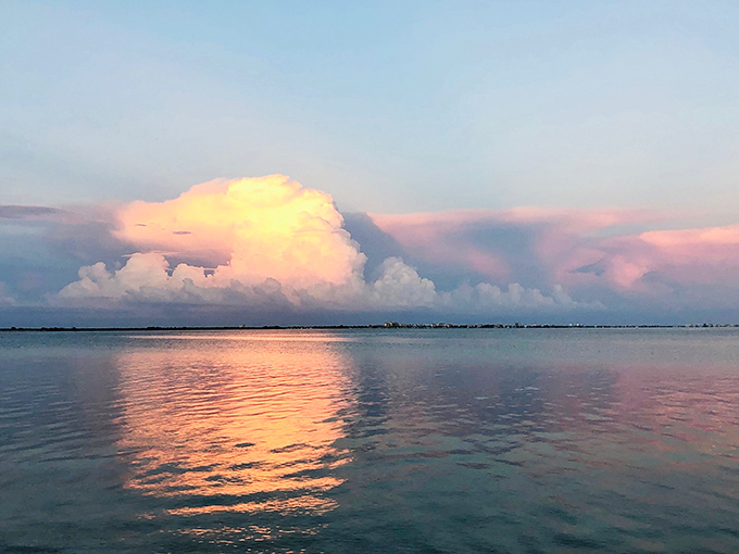 Sunset transforms the bay into a canvas of pinks and golds, while clouds build dramatic castles in the sky that reflect perfectly in the still water below.