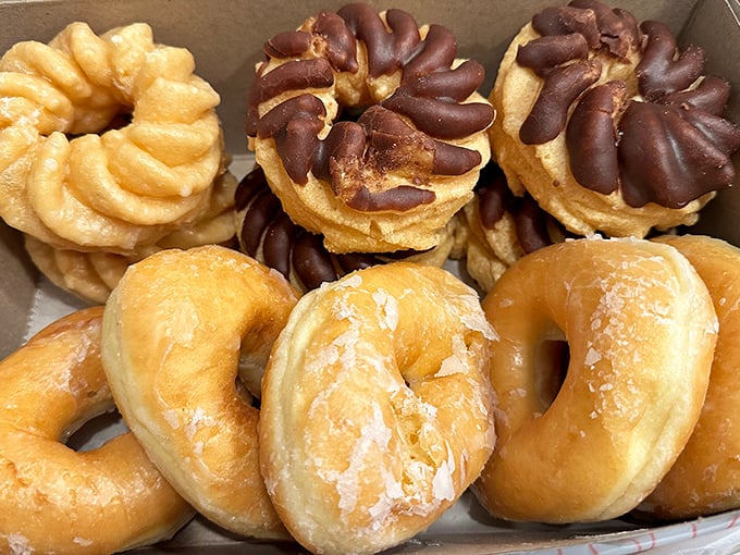 Crullers and glazed donuts nestled together like old friends. The glaze catching light like morning dew on pastry perfection.