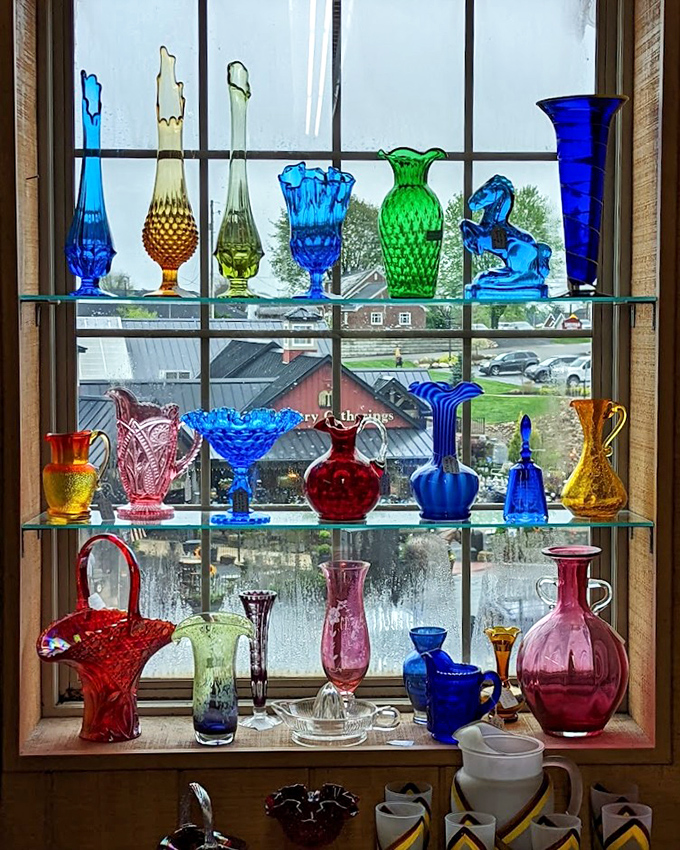 Sunlight streams through colored glass treasures, creating a stained-glass effect that transforms ordinary window shopping into a cathedral-like experience.
