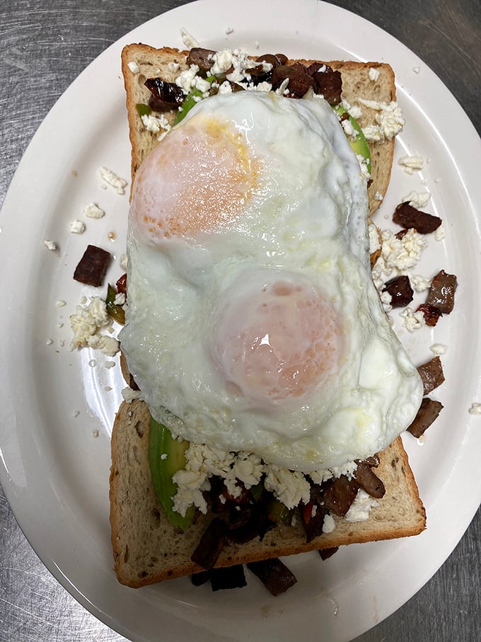 Two sunny-side up eggs perched atop a throne of toast, avocado, and savory bits&mdash;breakfast royalty if I've ever seen it.