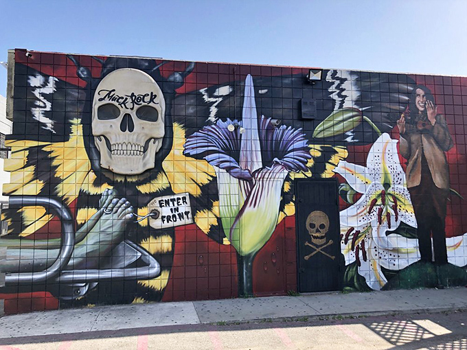 A vibrant street mural featuring winged skulls and flowers invites passersby to "Enter From Front" into this temple of mortality.