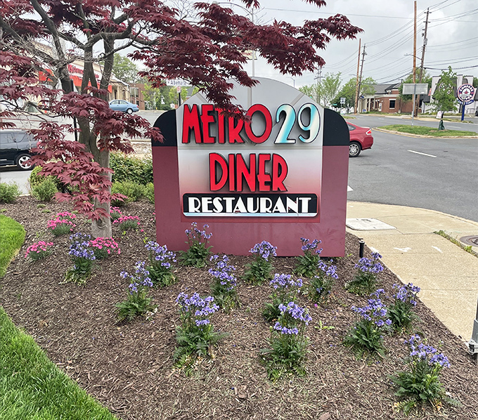 The roadside sign, surrounded by purple flowers, promises simple pleasures ahead&mdash;no fancy pretensions, just good food and warm welcomes.