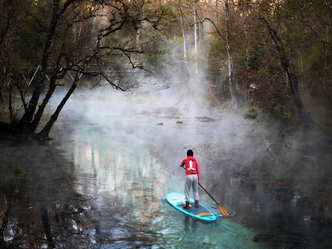 Paddleboarding through morning mist feels like gliding across another dimension. The red jacket pops against nature's dreamy filter.