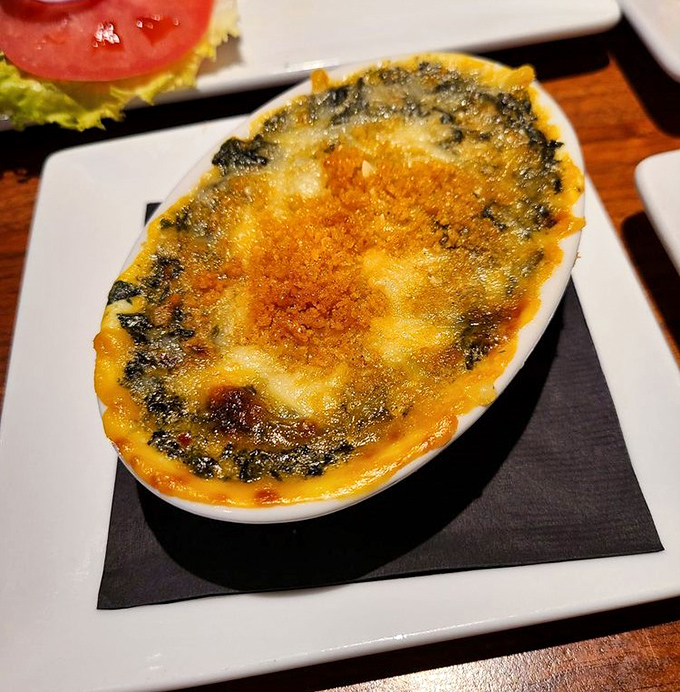 The Baked Spinach Maria arrives bubbling hot, its golden cheese crust hiding a creamy vegetable treasure that might convert lifelong spinach haters.