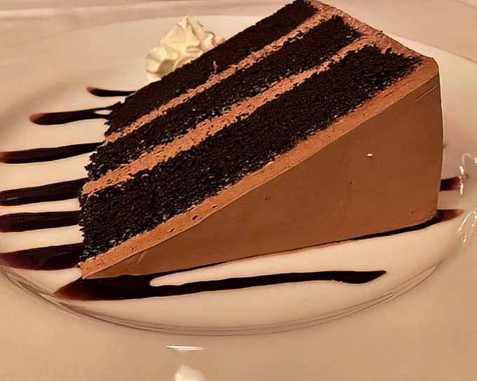 A slice of chocolate cake so imposing it deserves its own zip code &ndash; layers of dark decadence separated by creamy frosting.