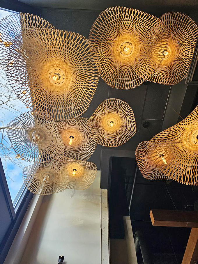 Intricate bamboo light fixtures cast a golden glow from above, transforming a simple ceiling into an artistic statement that demands attention.