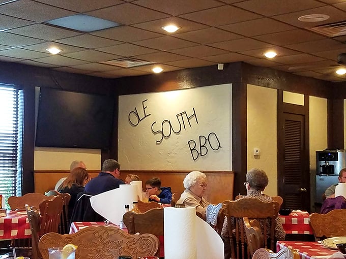The dining room wall proudly displays the Ole South BBQ name, while carved wooden chairs cradle generations of satisfied barbecue enthusiasts.