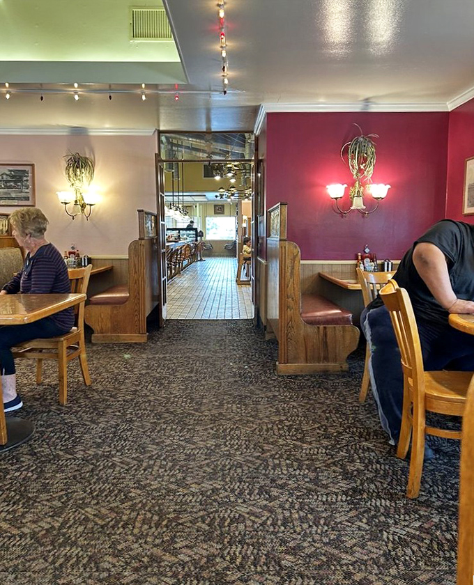 Burgundy walls, wooden booths, and warm lighting create distinct dining zones where regulars claim their territory and newcomers become converts.