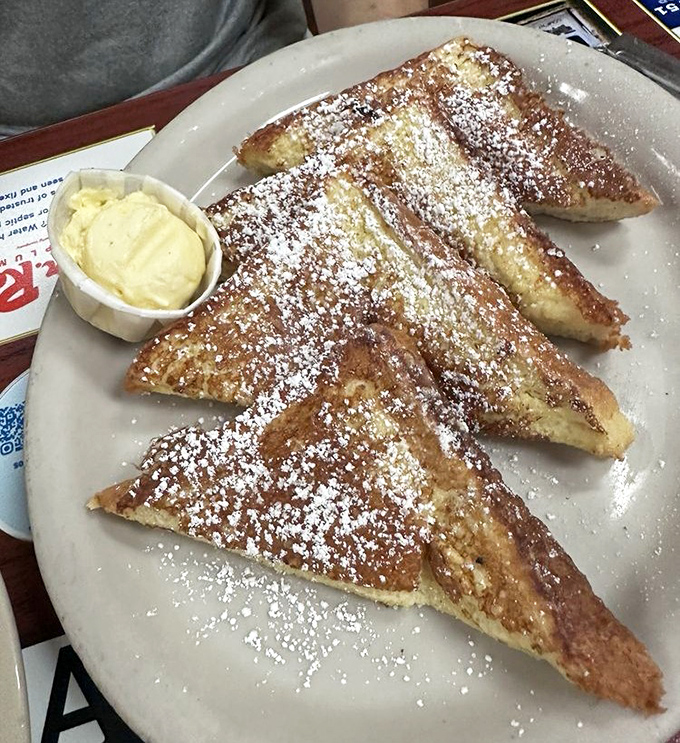 French toast dusted with powdered sugar like fresh snow on a delicious mountain. The butter cup on the side is just waiting to create a delicious avalanche.