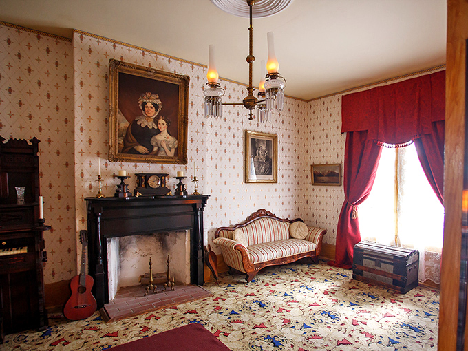 Rich burgundy drapes and period furniture create an elegant Victorian parlor where families once gathered for evening entertainment.