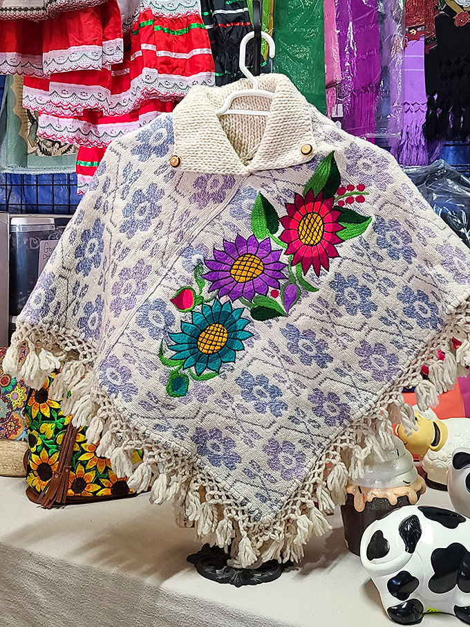 A beautifully embroidered Mexican poncho with vibrant sunflower designs hangs among traditional garments celebrating cultural heritage through textile art.