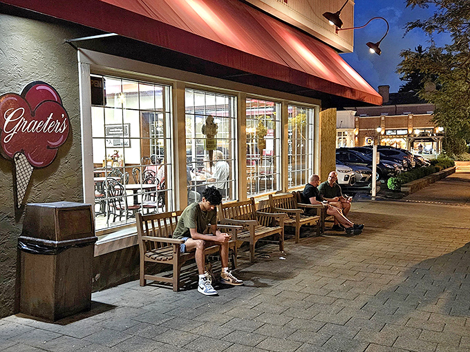 Evening at Graeter's transforms the sidewalk into a community gathering spot, where wooden benches welcome ice cream enthusiasts under the warm glow of storefront lights.