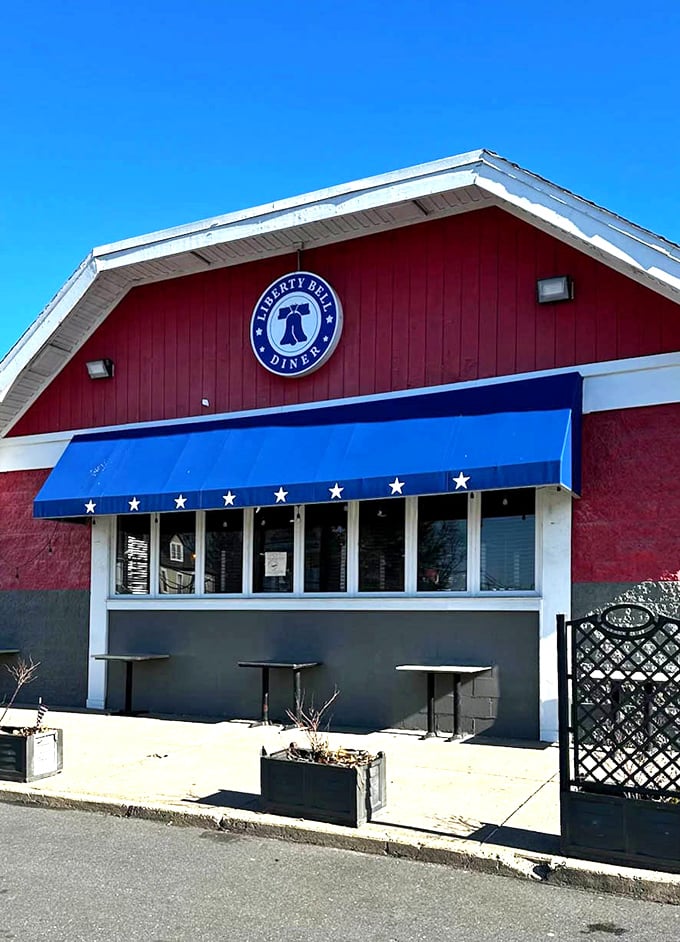 The diner's exterior on a perfect blue-sky day, beckoning hungry travelers like a patriotic lighthouse guiding ships to delicious shores.