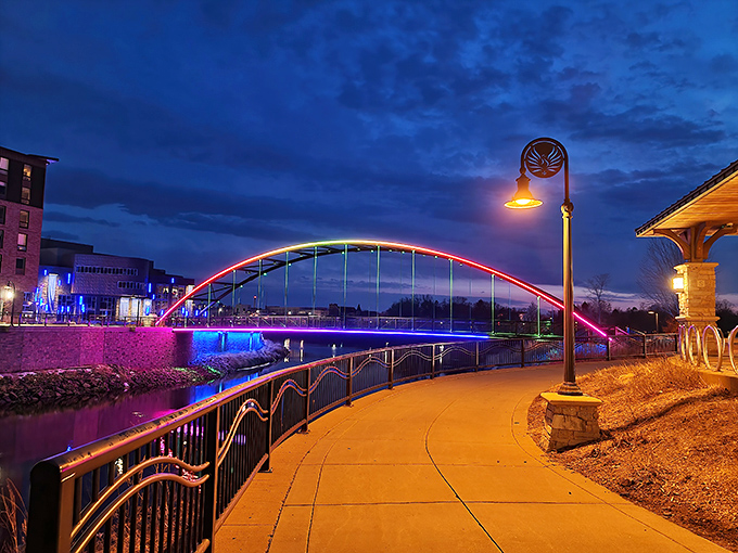 Phoenix Park's illuminated bridge transforms into a rainbow at night, its colors reflecting on the water like Eau Claire showing off its artistic side after dark.