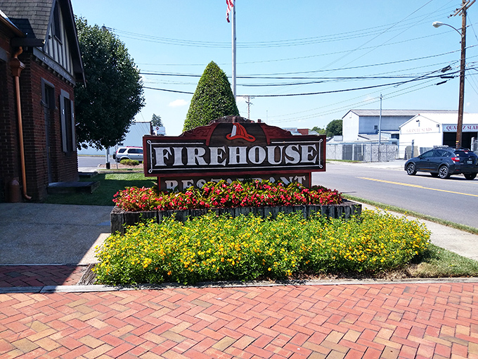 The Firehouse sign, surrounded by seasonal blooms, stands as a colorful roadside promise of smoky delights waiting just beyond the brick facade.