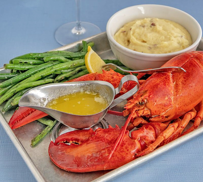 A perfectly steamed lobster flanked by green beans and mashed potatoes. The silver sauce boat holds liquid gold&mdash;clarified butter for dunking.